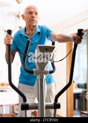 Positive senior man works out on an elliptical machine at home Stock ...