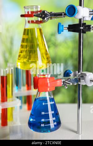 Retort stand and laboratory flasks with liquids on grey background ...