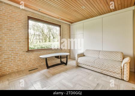 Comfortable couch located near carpet and table against window in ...