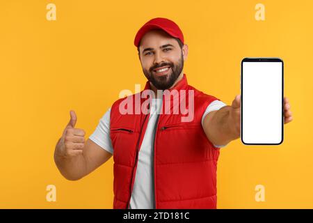 Happy courier holding smartphone with empty screen and showing thumbs ...