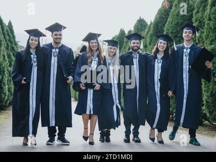Faculty students celebrate graduation in the park, smiling and hugging ...