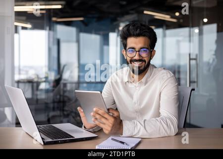 Hispanic man with beard using touchpad sitting on the sofa smiling ...