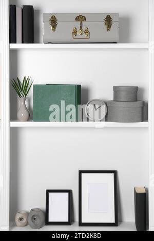 White shelves with clock, photo frames and different decor indoors ...
