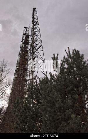 Tall metal radar tower standing amidst lush greenery under a cloudy sky ...