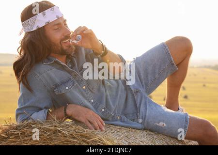 Hippie man smoking joint on hay bale in field Stock Photo - Alamy