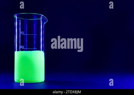 Laboratory beaker with luminous liquid on dark blue background, space ...