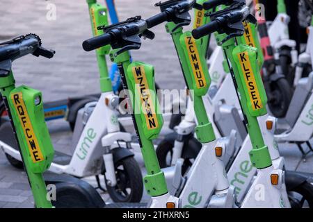 A line of electric scooters from Lime, Dott and Tier for hire / rental parked on a pavement in ...