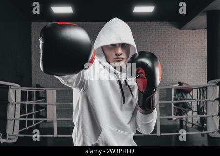 Brutal athlete boxing in the ring in a white hoodie covered with a hood ...