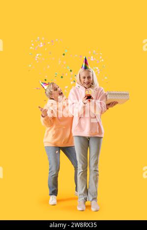 Mature woman with birthday muffin and confetti on light background ...