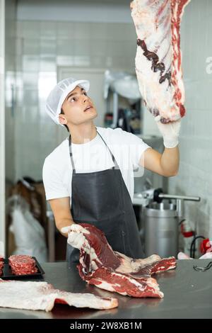 Positive young salesman demonstrating piece of meat in butcher shop ...
