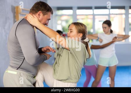 Tween girl performing knee strike in midsection to instructor in self ...