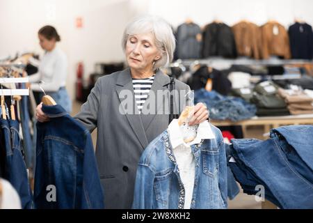 Old woman customer choosing jean jacket in clothing store Stock Photo ...