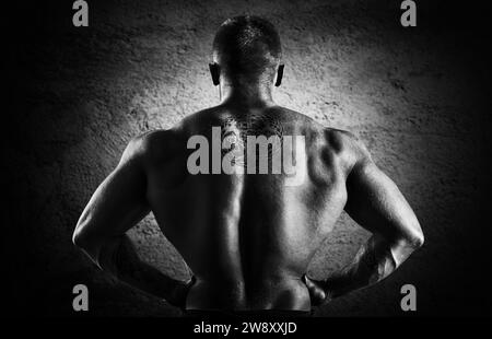 Huge weightlifter stands with his back to the camera and shows his huge ...