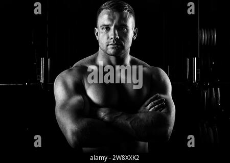 The weightlifter is posing in front of the camera with his arms crossed ...