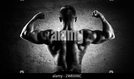 Huge weightlifter is standing with his back to the camera and straining ...