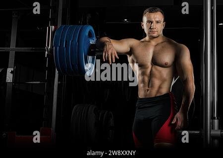 The weightlifter leans his hand on the barbell and looks menacingly ...