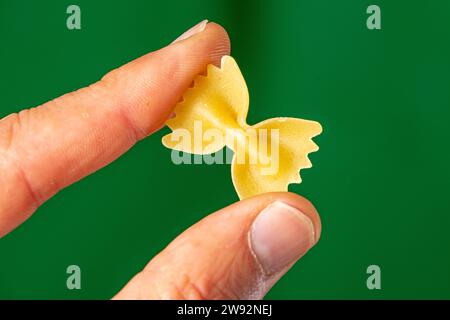 loop-shaped food wheat pasta between fingers under green background ...