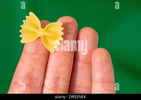 loop-shaped food wheat pasta between fingers under green background ...