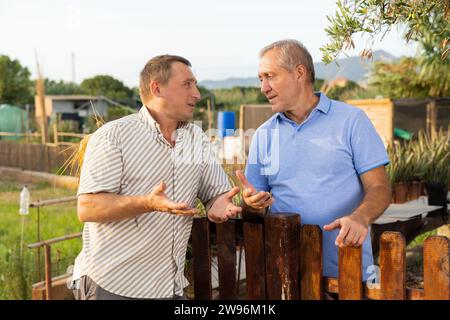 Neighbors standing at fence outdoors and having conversation. Village ...