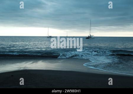 A serene beach scene at dusk with the sun setting over the ocean ...
