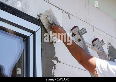 A closeup of a person applying cement on a brick with a spatula in a ...