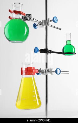 Retort stand and laboratory flasks with liquids on grey background ...