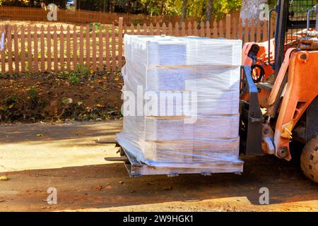 Worker at small forklift unloading lifts pallet concrete blocks for ...