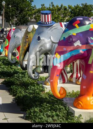 An exhibit of artistically painted elephants decorates a sidewalk in ...