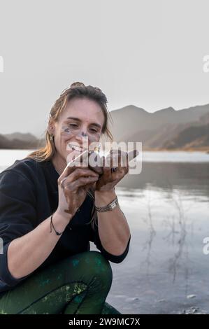Woman putting mud on hands and face while enjoying outdoors in nature ...