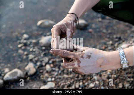 Woman putting mud on hands and face while enjoying outdoors in nature ...
