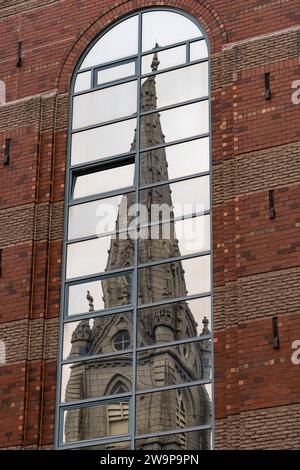 Church steeple reflects on a tall arched window of a brick building in ...