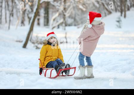 Little girl pulling sledge with her brother through snow in winter park ...
