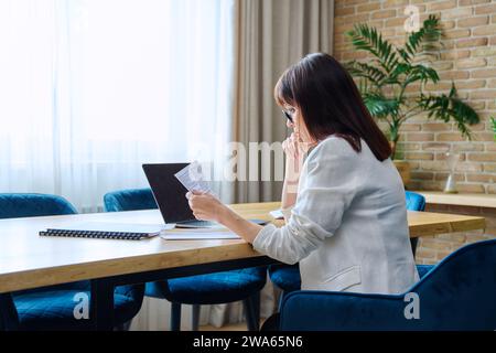 Serious mature businesswoman reading official letter, sitting in office ...