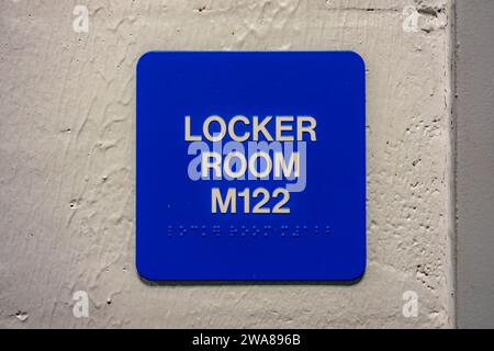 Blue LOCKER ROOM M122 sign with braille, on a white block wall Stock ...