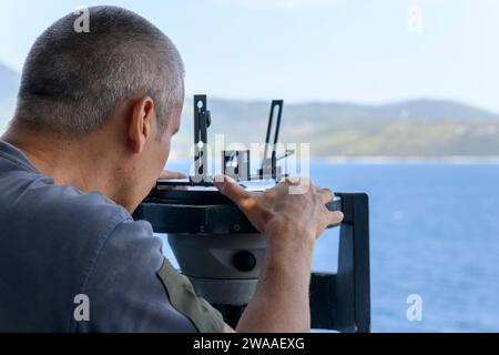Navigational officer taking bearing with azimuth ring on gyro compass ...