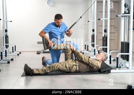 Physiotherapist helps military man perform exercises to stretch his leg ...