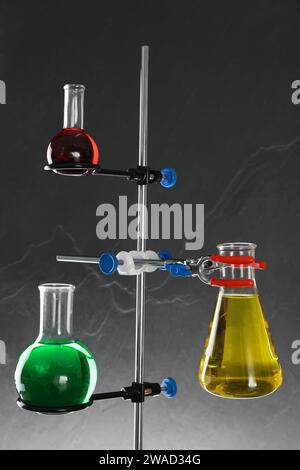 Retort stand and laboratory flasks with liquids on grey background ...