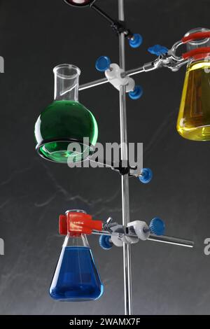 Retort stand and laboratory flasks with liquids on grey background ...