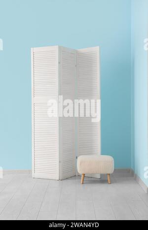 Modern ottoman and folding screen near light wall Stock Photo - Alamy