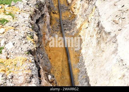 A plastic black gas pipe at the bottom of the trench. A dug trench for ...