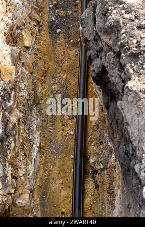 A plastic black gas pipe at the bottom of the trench. A dug trench for ...