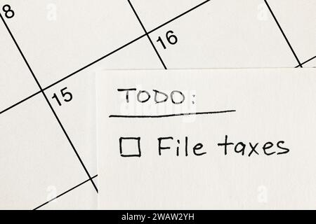 Hand written to-do list with 'File taxes' reminder written on a sticky ...