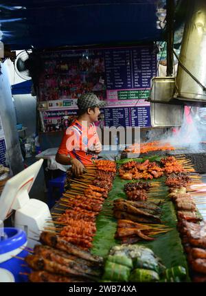A Thai man grilling chicken at a small street food on Soi Naradhiwas ...