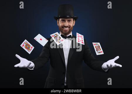 Smiling magician showing trick with cards on dark blue background Stock ...