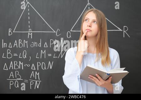 Pondering math teacher with book near blackboard in classroom Stock ...