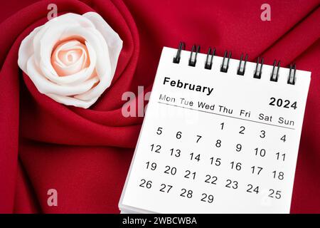 February 2024 desk calendar and pink rose petals on a red background ...