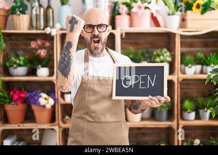Hispanic man with tattoos working at florist holding open sign with ...