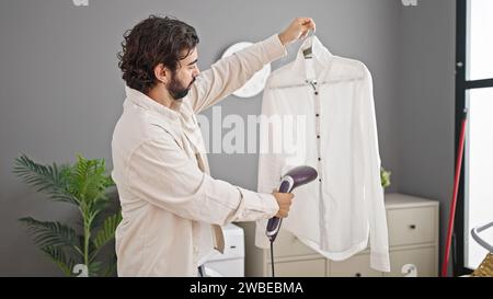 Young hispanic man with beard ironing clothes at home smiling with an ...