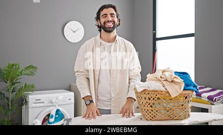 Young hispanic man with beard ironing clothes at home thinking ...