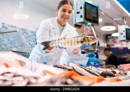 Positive saleswoman demonstrating seabass in fish store Stock Photo - Alamy
